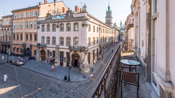 Uma rua de paralelepípedos com edifícios históricos, uma linha de bonde e uma varanda com móveis de vime.