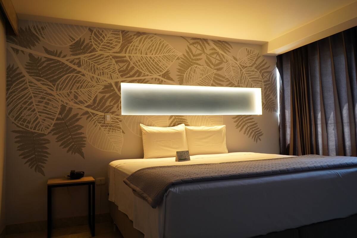 Quarto de hotel com cama, mesa de cabeceira, televisão na parede e parede com padrão.