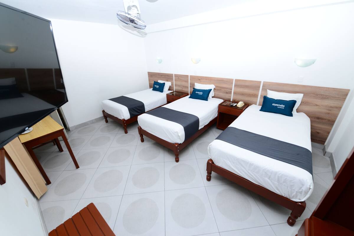 Quarto de hotel com três camas, uma mesa e uma televisão.