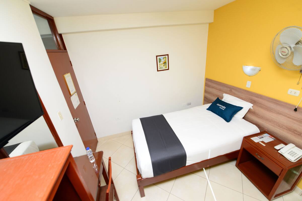 Quarto de hotel com cama, mesa de cabeceira e escrivaninha com cadeira.