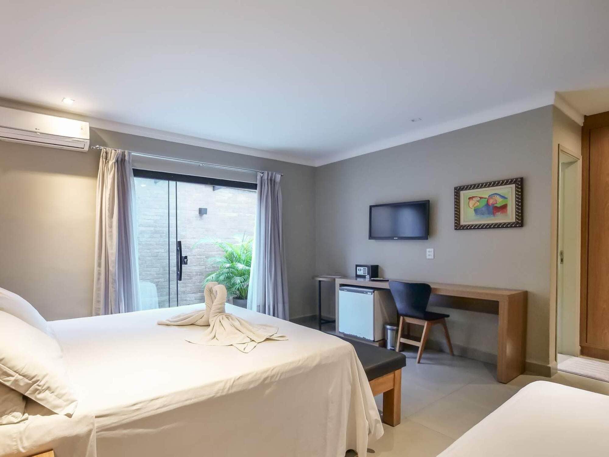 Quarto de hotel com cama, secretária, cadeira, televisão e porta.