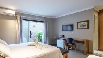 Quarto de hotel com cama, secretária, cadeira, televisão e porta.