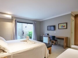 Quarto de hotel com cama, secretária, cadeira, televisão e porta.