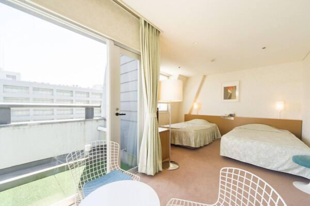 Quarto de hotel com varanda, cama, cadeira e mesa.