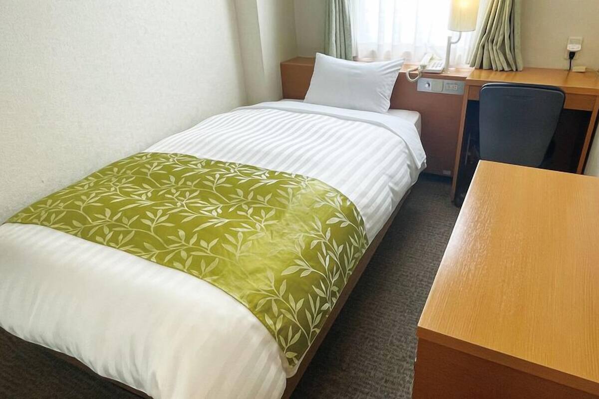 Quarto de hotel com cama, escrivaninha e cadeira.