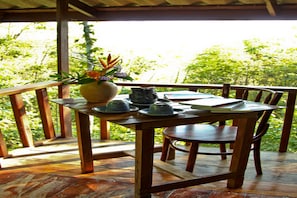 Mesa de madeira com um vaso de flores, um jarro e um livro em um deck com guarda-corpo.