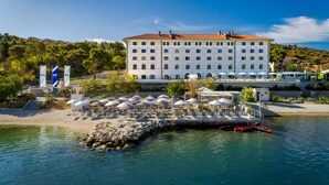 Um hotel grande com terraço à beira-mar, mesas ao ar livre e um cais com barcos.