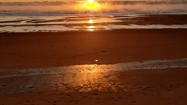 Uma praia com pôr do sol, ondas e céu claro.