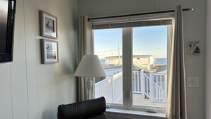 Quarto com vista para um cais e o mar, uma poltrona de couro preto, uma luminária e uma placa com a inscrição 'Welcome'.