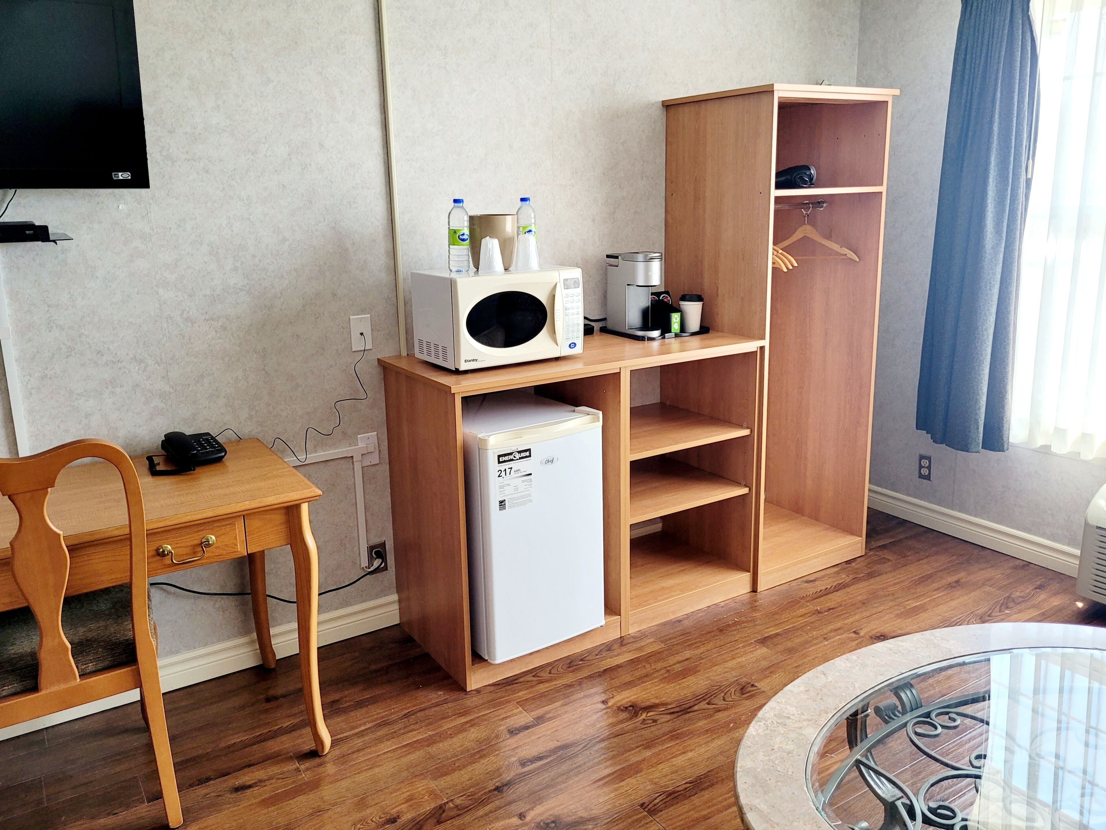 Quarto compacto com escrivaninha de madeira, mini-geladeira, micro-ondas e armário.