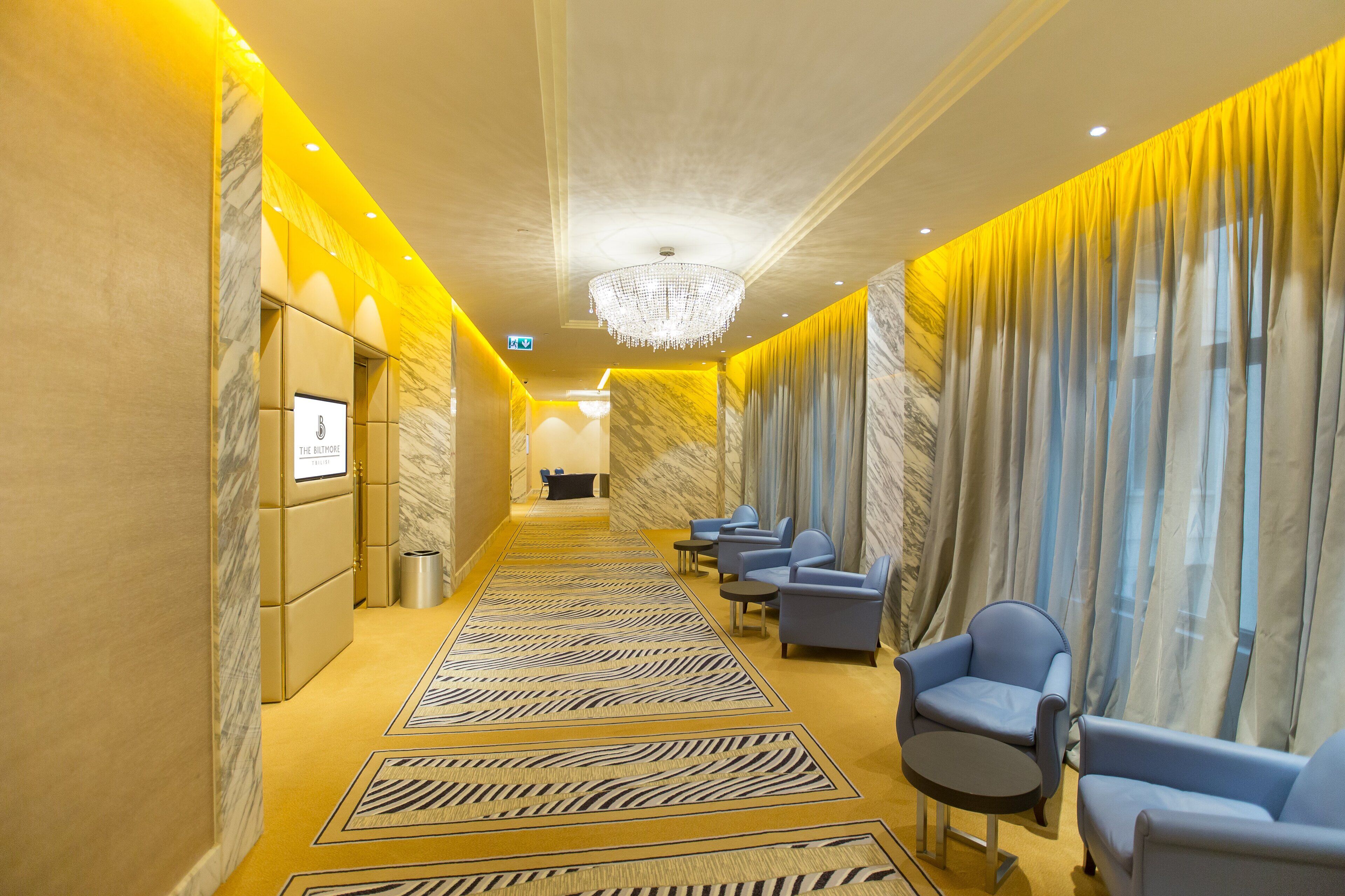 Um corredor de hotel com carpete estampado em zebra, poltronas azuis e um lustre.