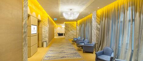 Um corredor de hotel com carpete estampado em zebra, poltronas azuis e um lustre.