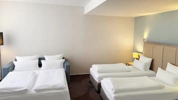 Quarto de hotel com duas camas de solteiro, um sofá e uma mesa pequena.
