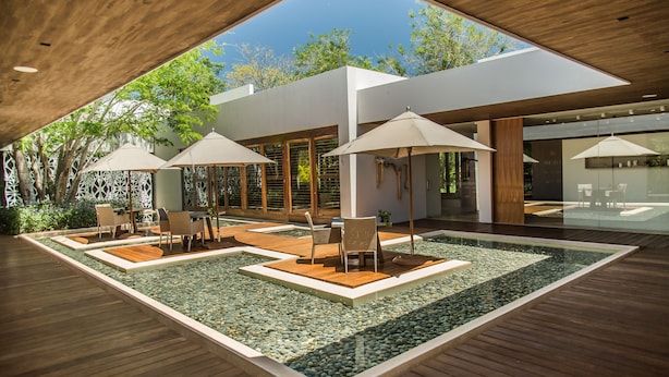 Um pátio moderno ao ar livre com piscina retangular, piso de madeira e área de estar externa com guarda-sóis.
