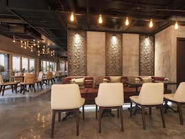Um restaurante com interior moderno, apresentando uma área central com sofás e cadeiras, e um bar com mesas e cadeiras.