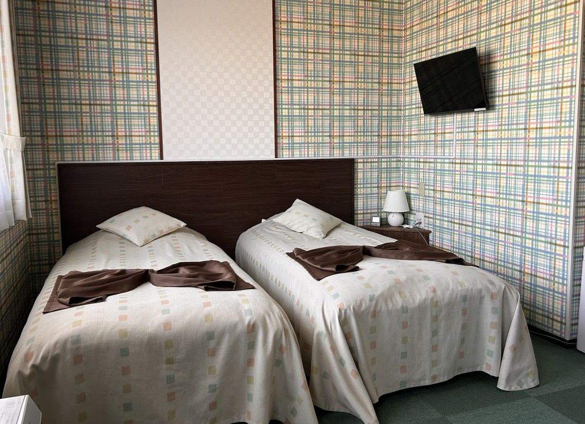 Quarto de hotel com duas camas, televisão presa na parede e papel de parede estampado.