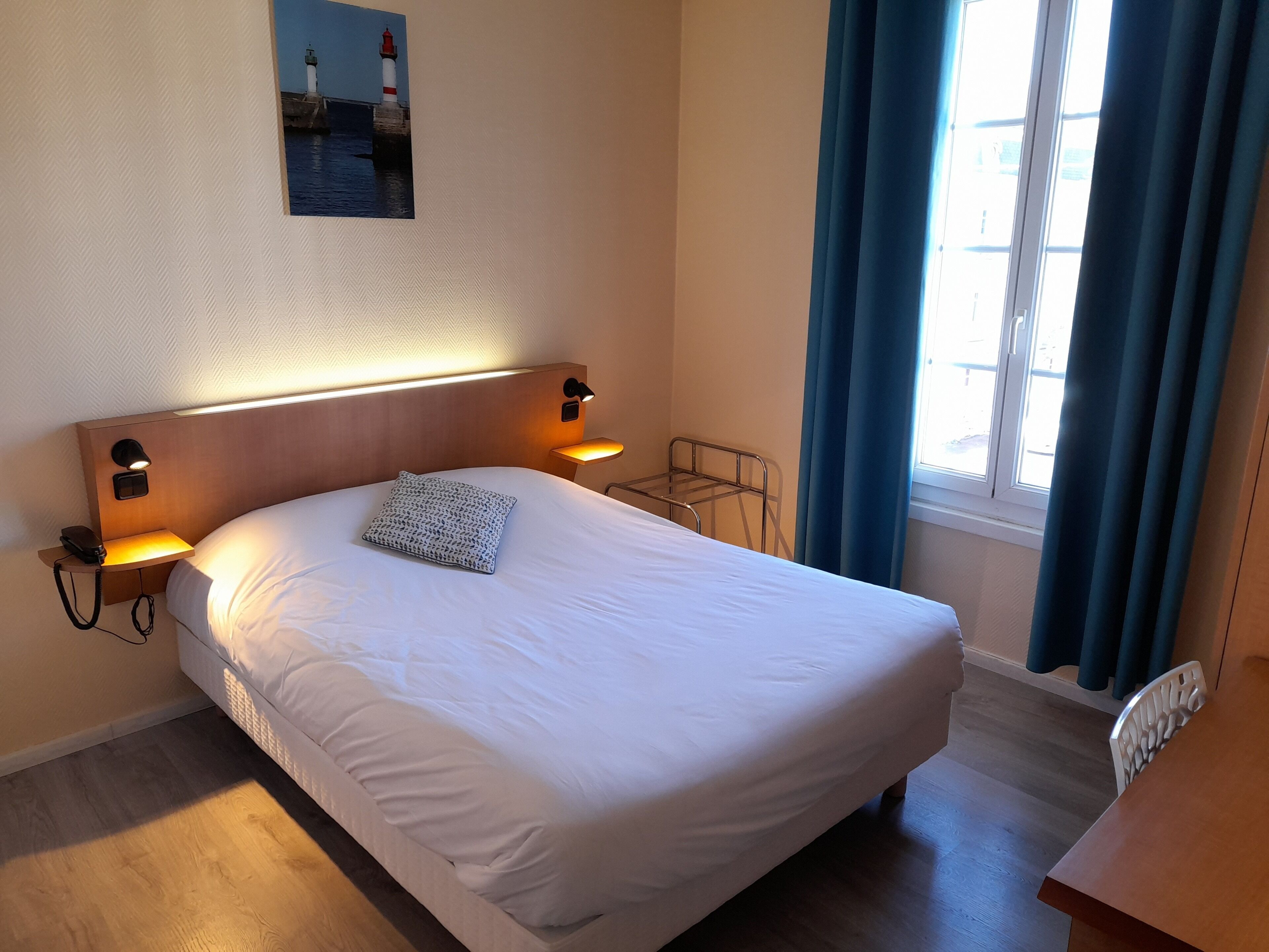 Uma cama bem arrumada com travesseiro, luminárias de cabeceira, mesa de cabeceira e uma janela com cortinas.