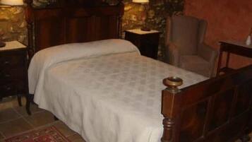 Quarto com cama de madeira, duas mesas de cabeceira com luminárias, uma cadeira e uma parede de pedra.