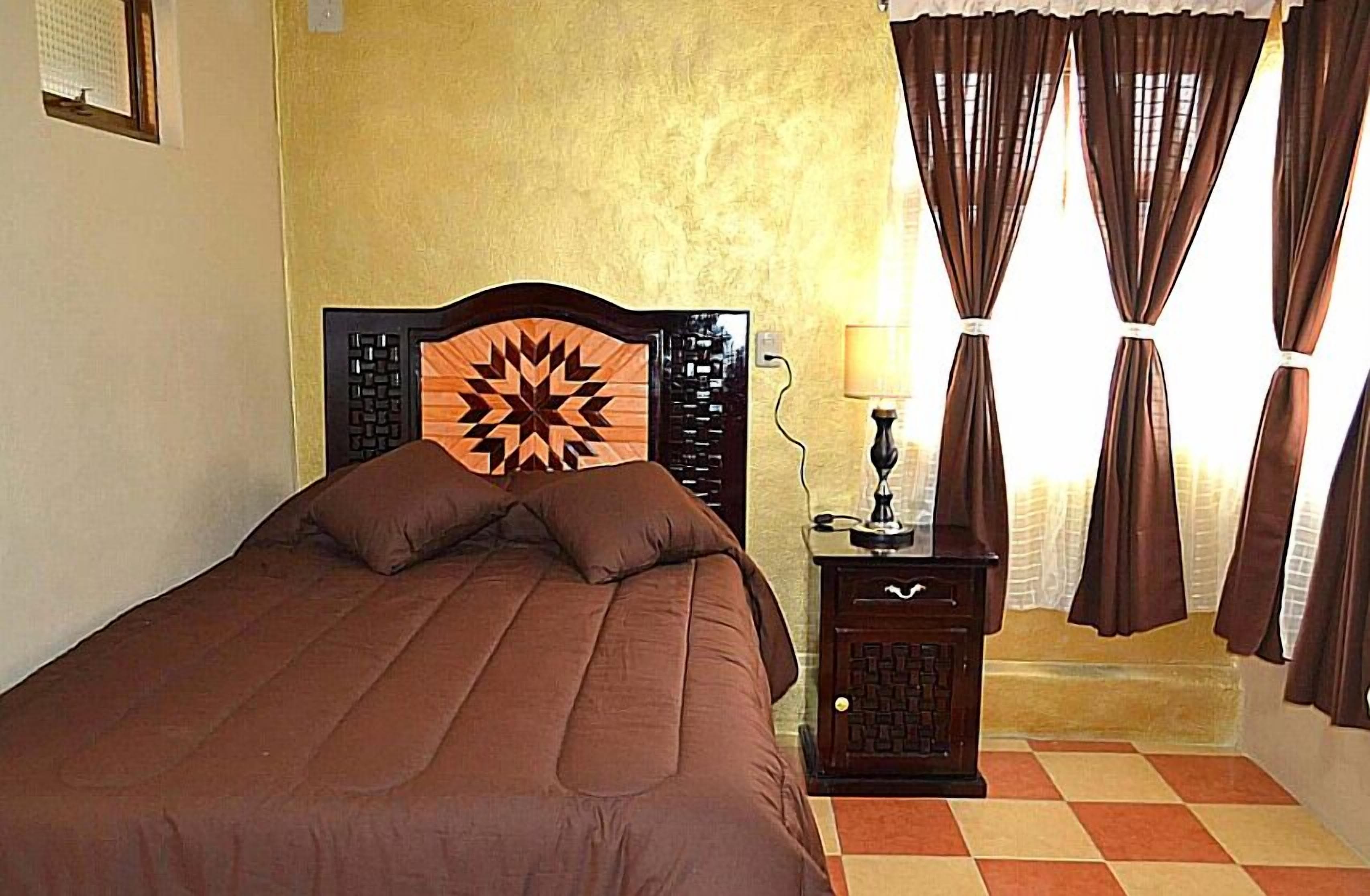 Um quarto com cama, mesa de cabeceira, luminária e cortinas.