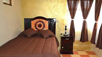 Um quarto com cama, mesa de cabeceira, luminária e cortinas.