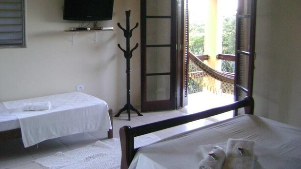 Quarto com duas camas, televisão e varanda com rede.