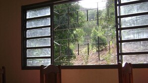 Quarto com uma janela grande, cadeiras de madeira, uma mesa com toalha xadrez e uma pequena planta na mesa.