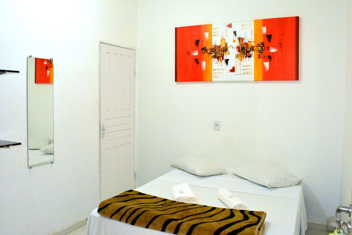 Quarto com uma cama, um espelho e um quadro na parede.