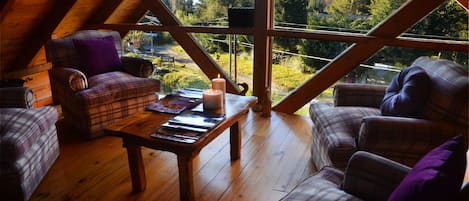 Quarto de loft aconchegante com teto de madeira e grandes janelas com vista para as montanhas.