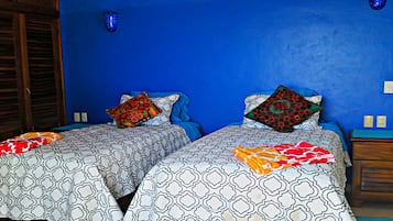 Quarto com duas camas, cada uma com roupa de cama e almofadas estampadas, parede azul e mesa de cabeceira de madeira com abajur.