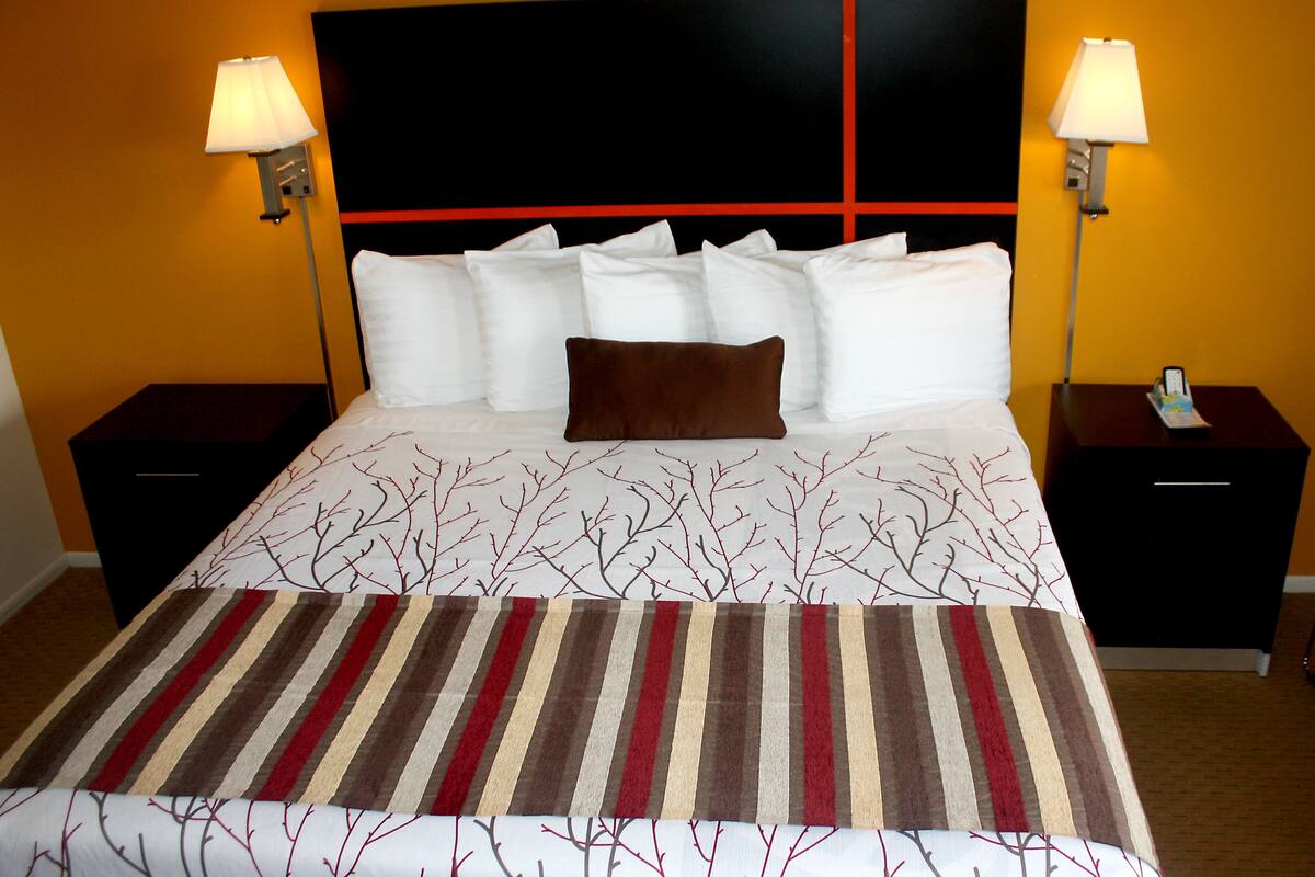 Quarto de hotel com uma cama grande, duas mesinhas de cabeceira e cabeceira com detalhe vermelho.