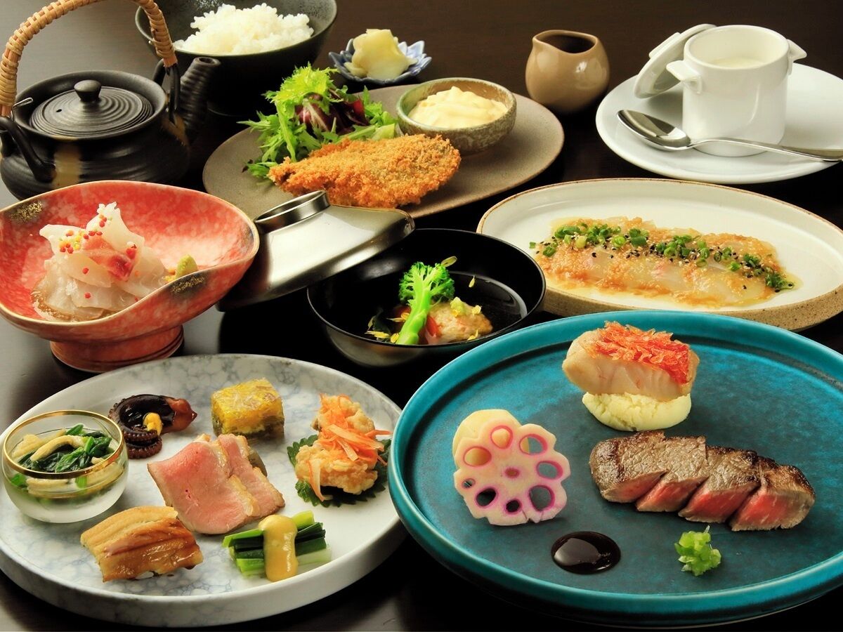 Diversos pratos sobre uma mesa, incluindo uma tigela de arroz, um prato de sashimi e um prato decorado com uma flor de lótus.