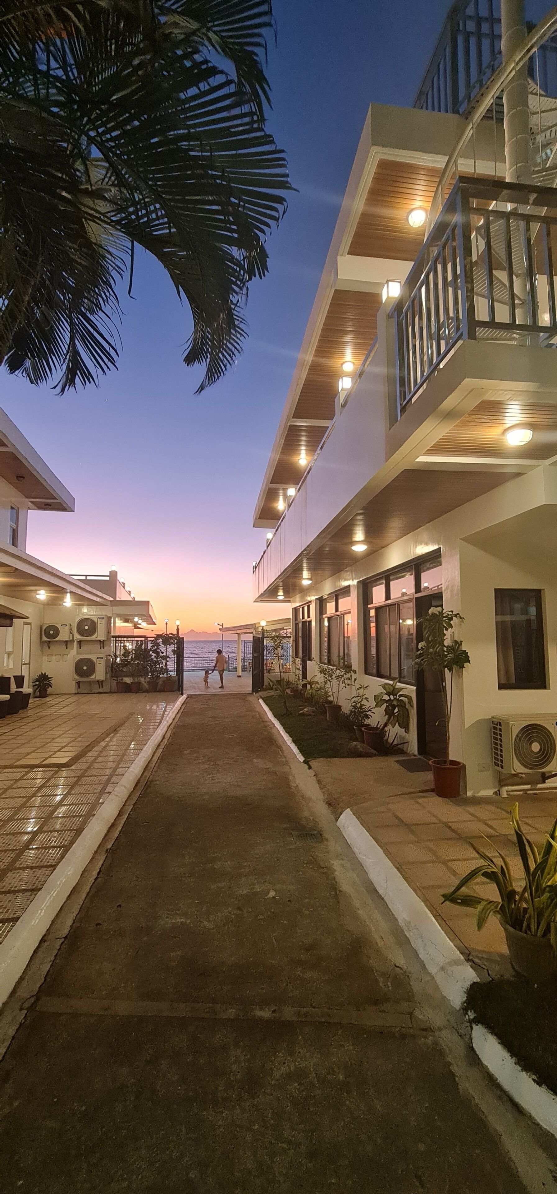 Um edifício com galeria coberta que dá para o mar, rodeado por vasos de plantas e áreas de estar ao ar livre.