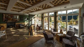 Um quarto amplo com grandes janelas, vigas de madeira no teto e diversas opções de assento, incluindo cadeiras e sofás.