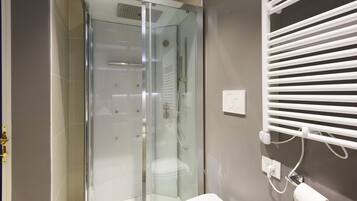 Um banheiro moderno com chuveiro de vidro, vaso sanitário branco e porta-toalhas.