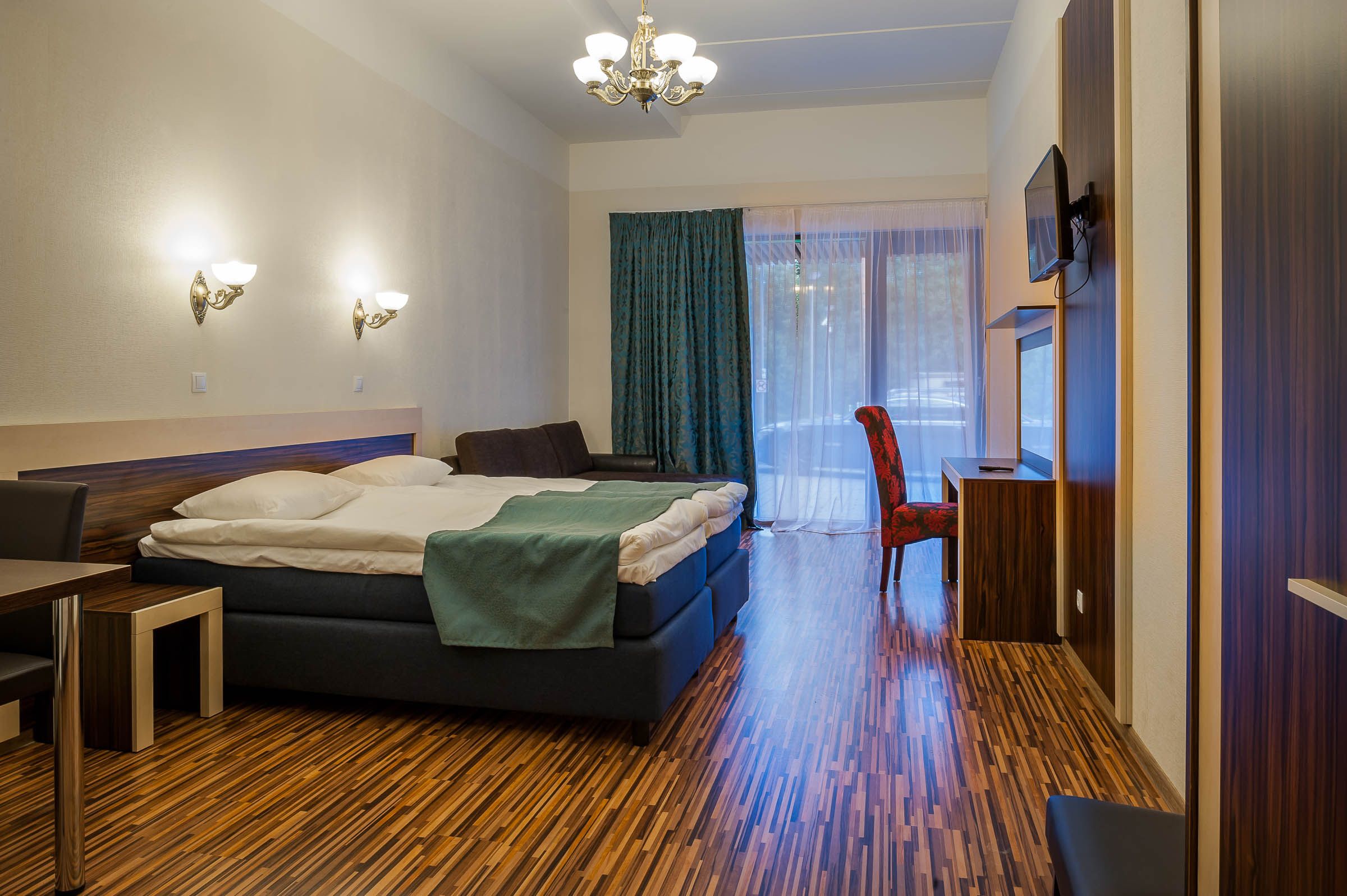 Quarto de hotel com cama, escrivaninha, cadeira, televisão e janela com cortinas.