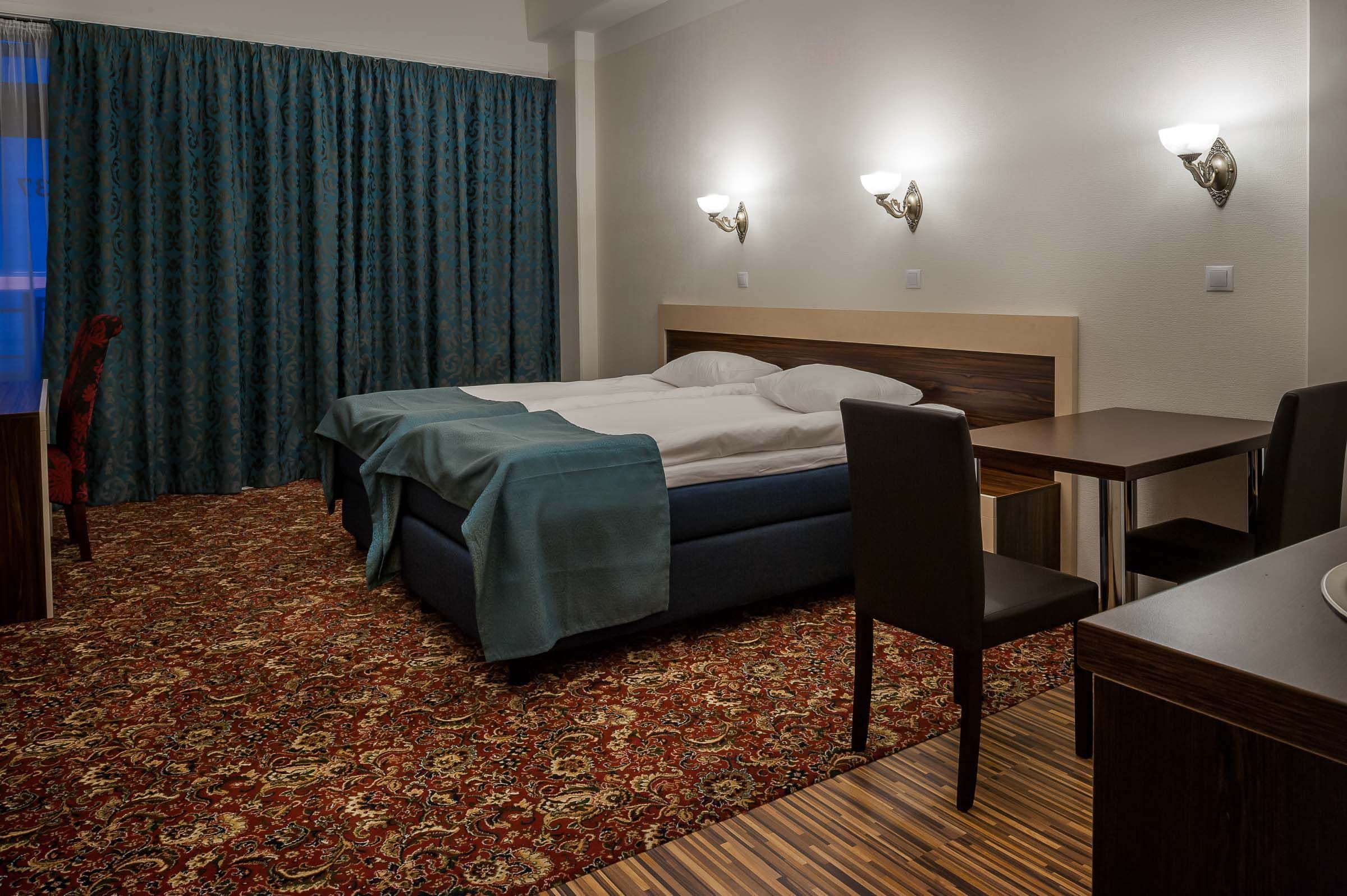 Quarto de hotel com cama, escrivaninha, cadeira e piso coberto por carpete.