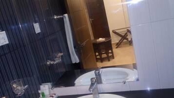 Casa de banho com uma pia branca, paredes revestidas de azulejos escuros e um espelho refletindo uma porta e uma cadeira.