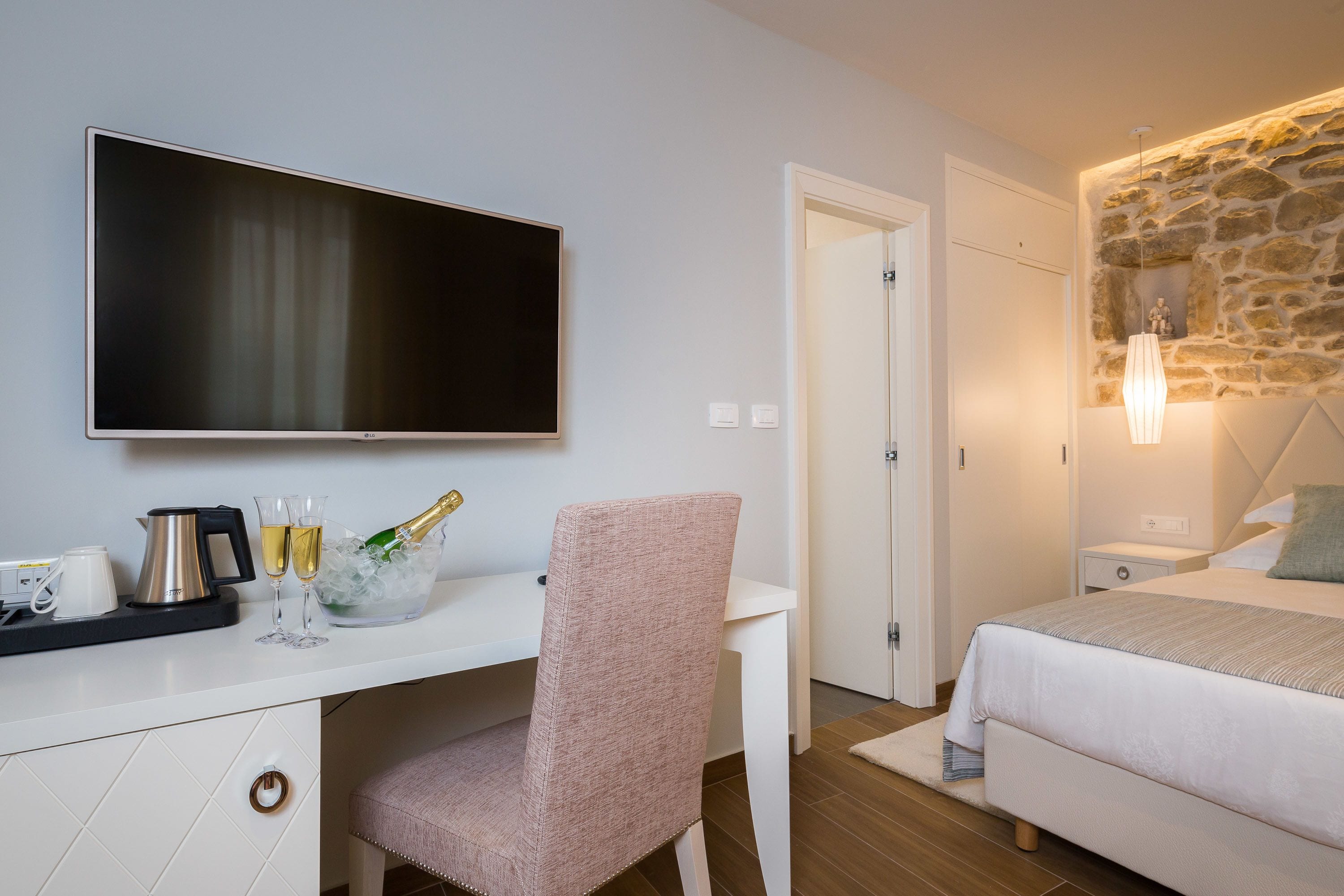Quarto de hotel com televisão de tela plana, uma escrivaninha com cadeira, uma cama e parede de pedra.