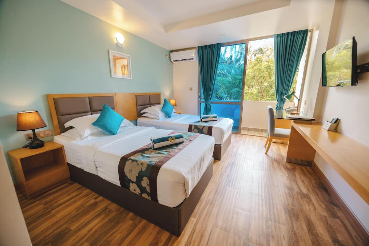 Quarto de hotel com duas camas, uma escrivaninha, uma cadeira, uma televisão e uma janela com cortinas.