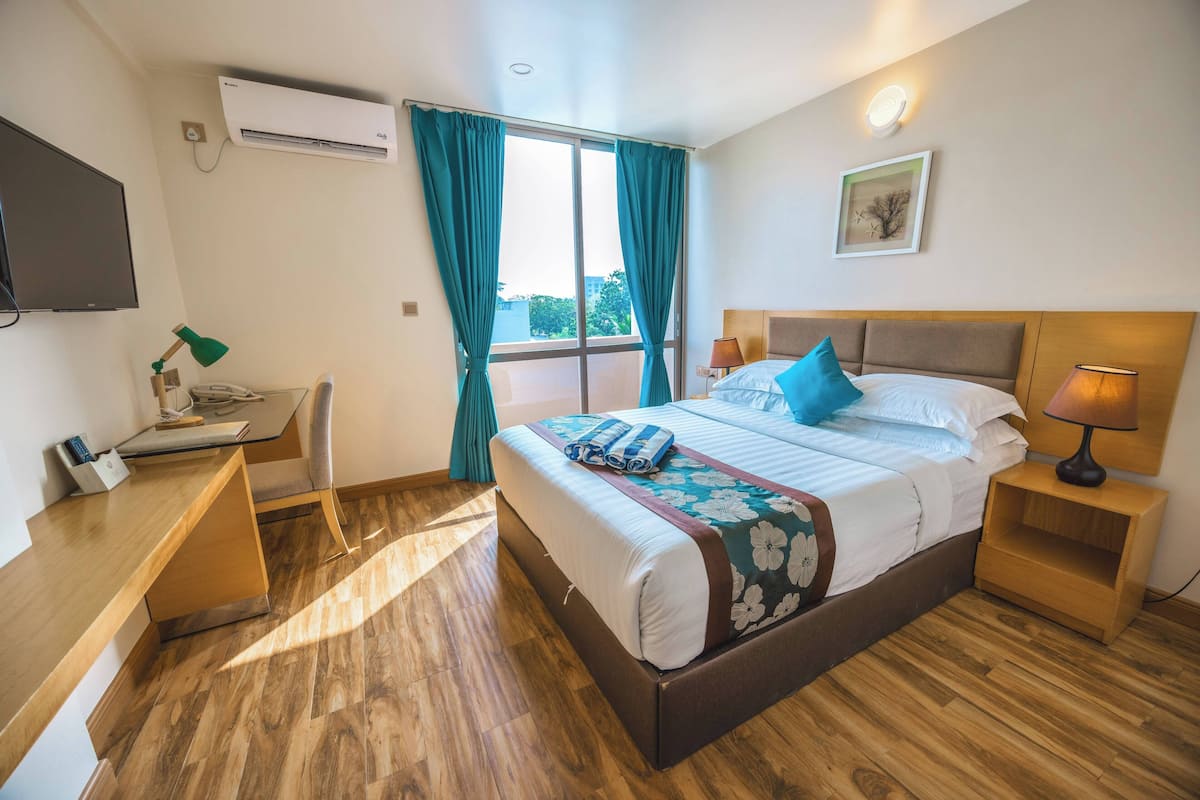 Quarto de hotel com cama, escrivaninha e janela.