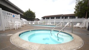 Piscina com borda azulejada, cercada por um muro branco e cadeiras de plástico brancas.