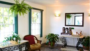 Quarto com mesa, cadeira, plantas em vasos, espaço para café e espelho na parede.