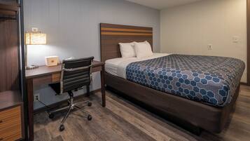 Quarto de hotel com escrivaninha de madeira, uma cadeira, cama com colcha estampada e mesa de cabeceira com abajur.