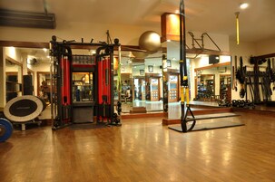 Academia com equipamentos de ginástica, espelho e piso de madeira.