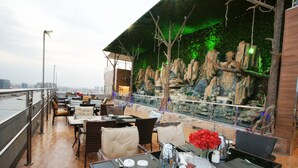 Restaurante no terraço com mesas ao ar livre, vista da cidade e um muro de pedras ao fundo.