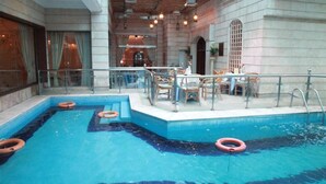 Piscina interior com água cristalina, rodeada por espreguiçadeiras e uma área de estar com mesas e cadeiras.