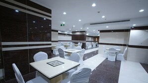 Uma sala de conferências com cadeiras e mesas brancas, dispostas em fileiras, chão liso e design moderno no teto.