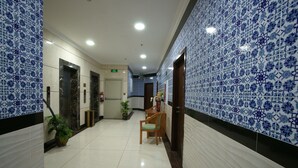 Um hall de hotel com piso de azulejos, dois elevadores, um balcão de recepção e plantas em vasos.