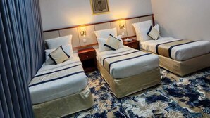 Quarto de hotel com três camas, carpete estampado, saída de ar no teto e luminárias fixadas na parede.