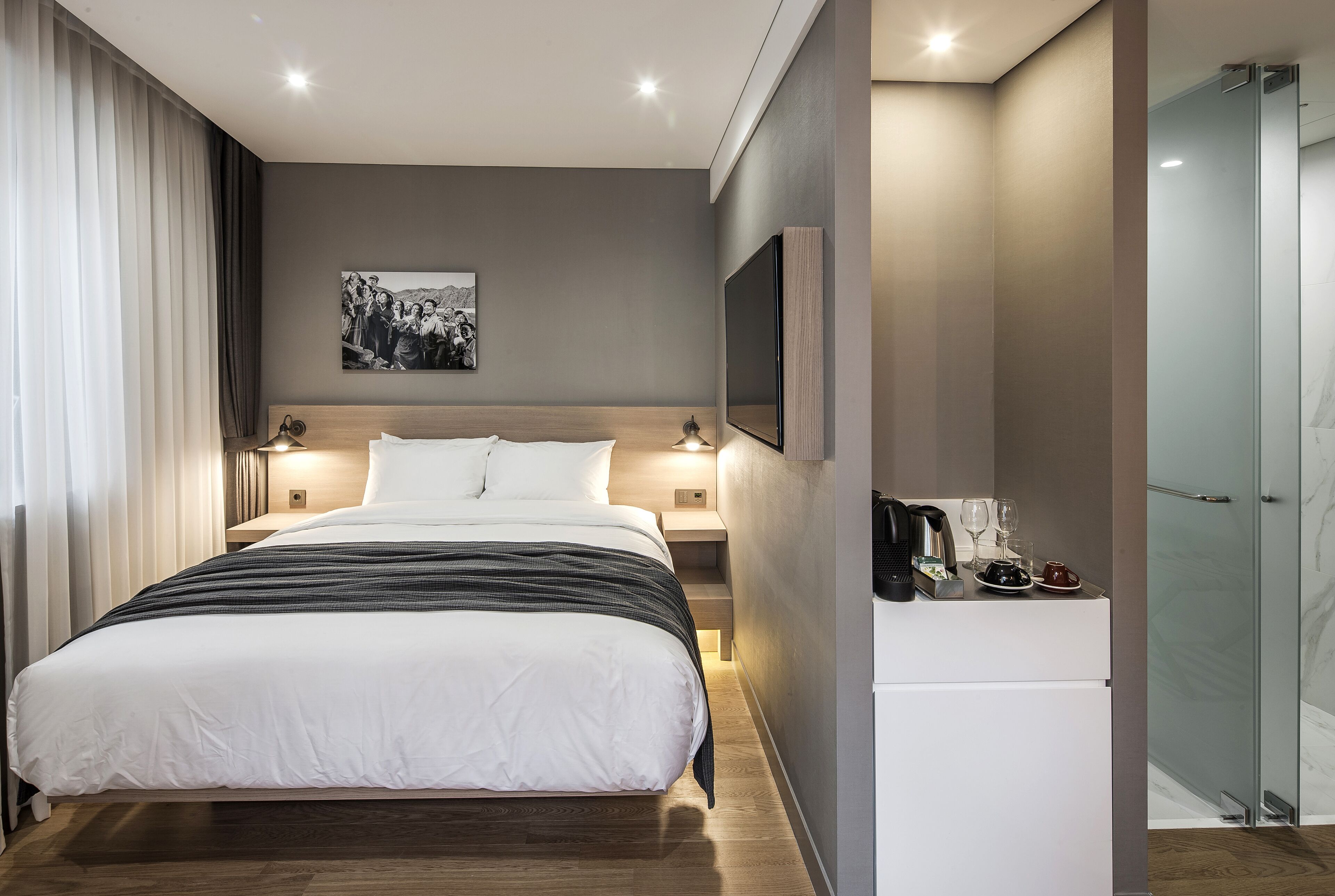 Quarto de hotel moderno com uma cama grande, televisão de tela plana, cafeteira e chuveiro de vidro.